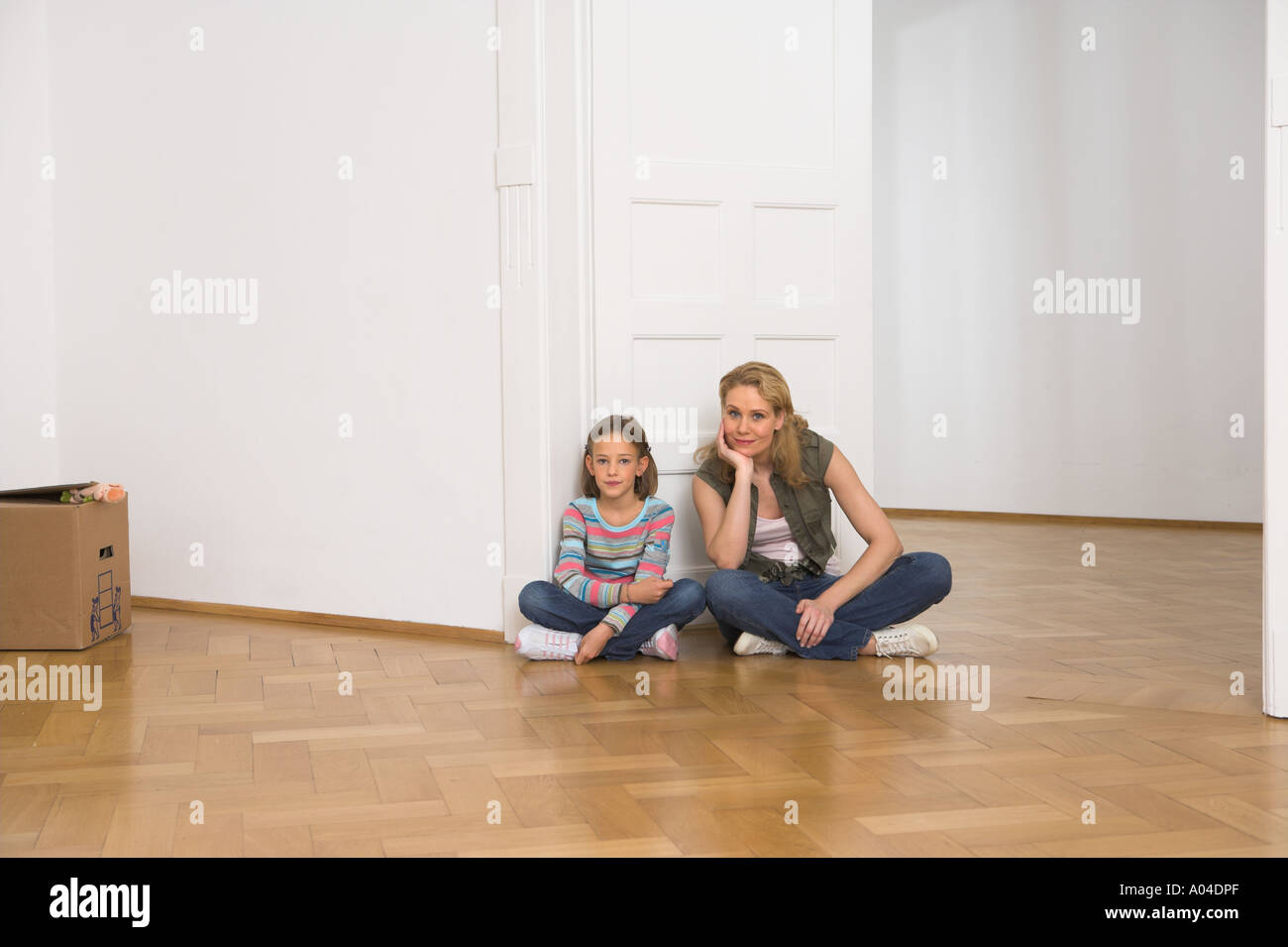 portrait of mother and daughter sitting together in empty room in new ...