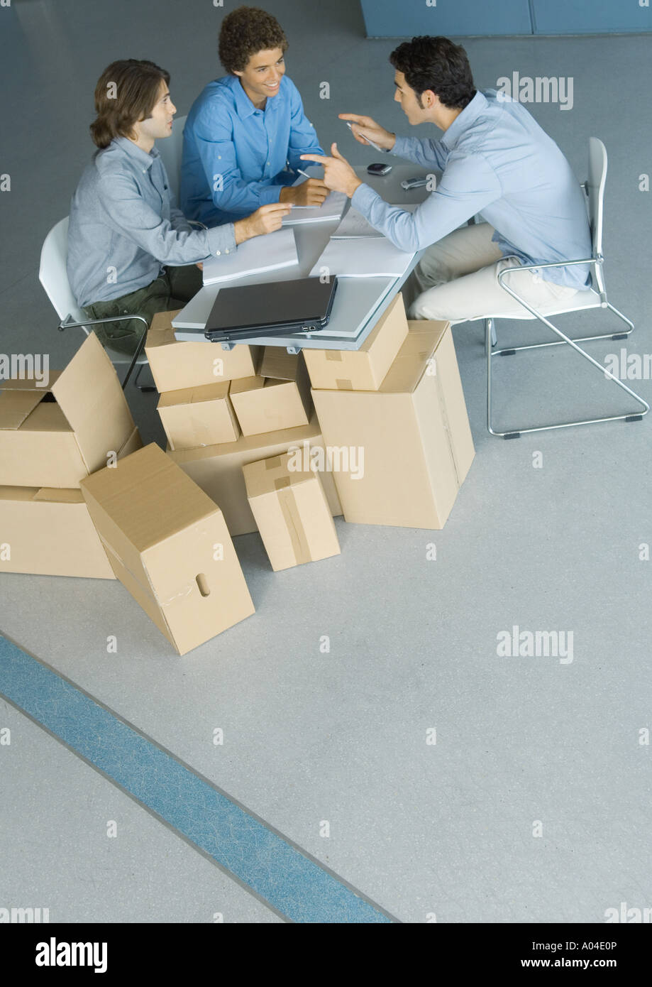 Businessmen sitting at table top supported by cardboard boxes, high ...