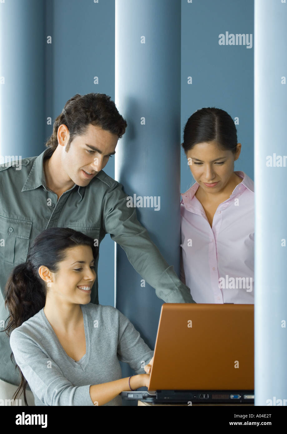 Three young adults using laptop computer together Stock Photo - Alamy