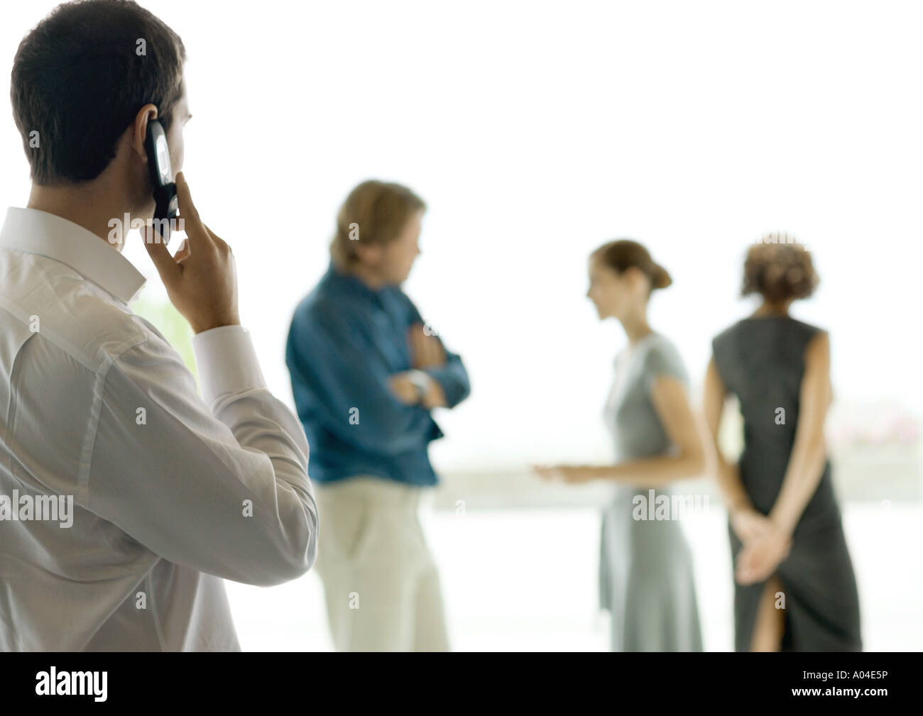 Man using cell phone, people standing and chatting in background Stock ...