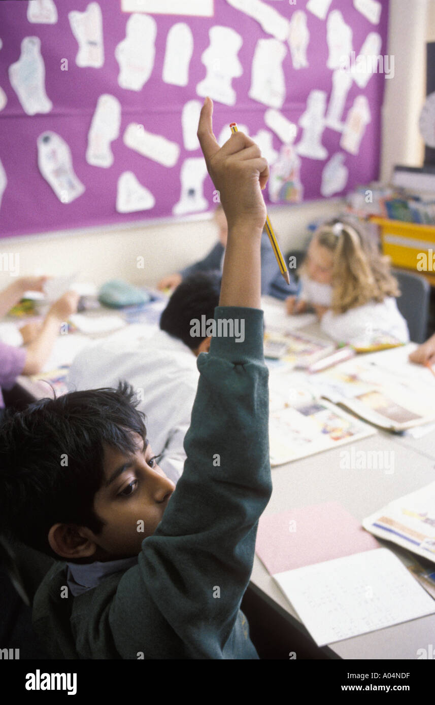 Child raising his hand to answer a question in primary school classroom ...