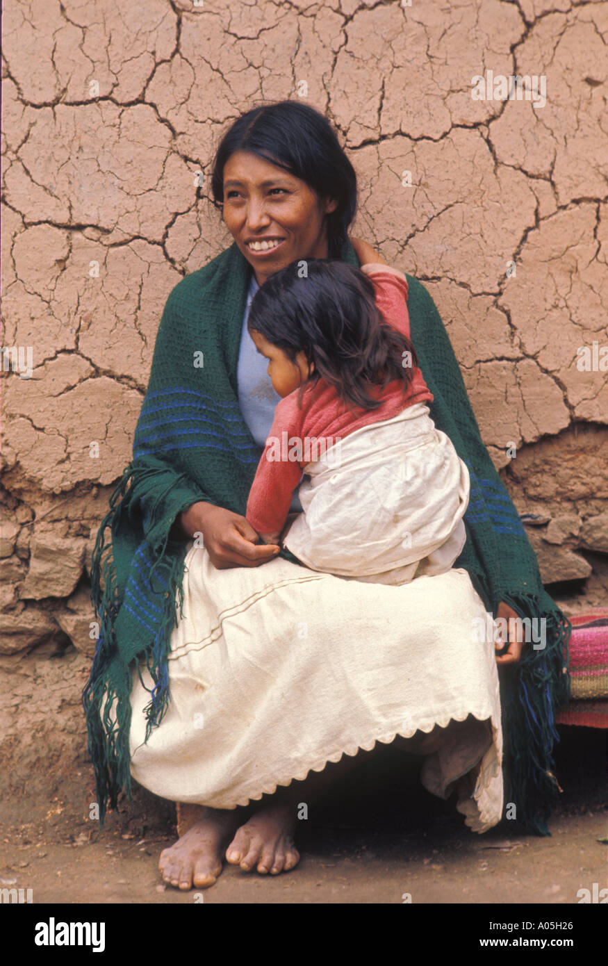 Bolivian Aymara Indian woman and baby sit beside a traditional mud wall ...