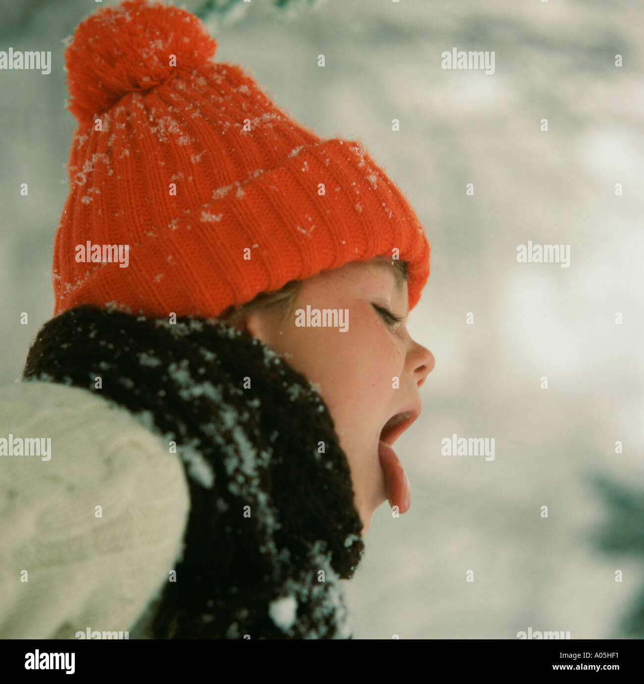 Little boy wearing a red winter cap outside in the snow sticking his ...