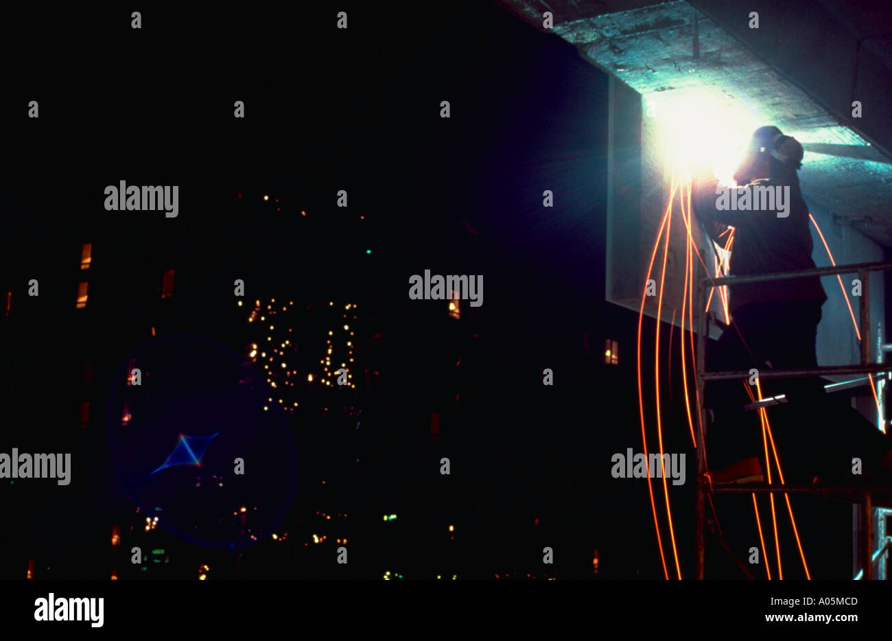 Sparks form ribbons of light as a construction welder works at night on ...