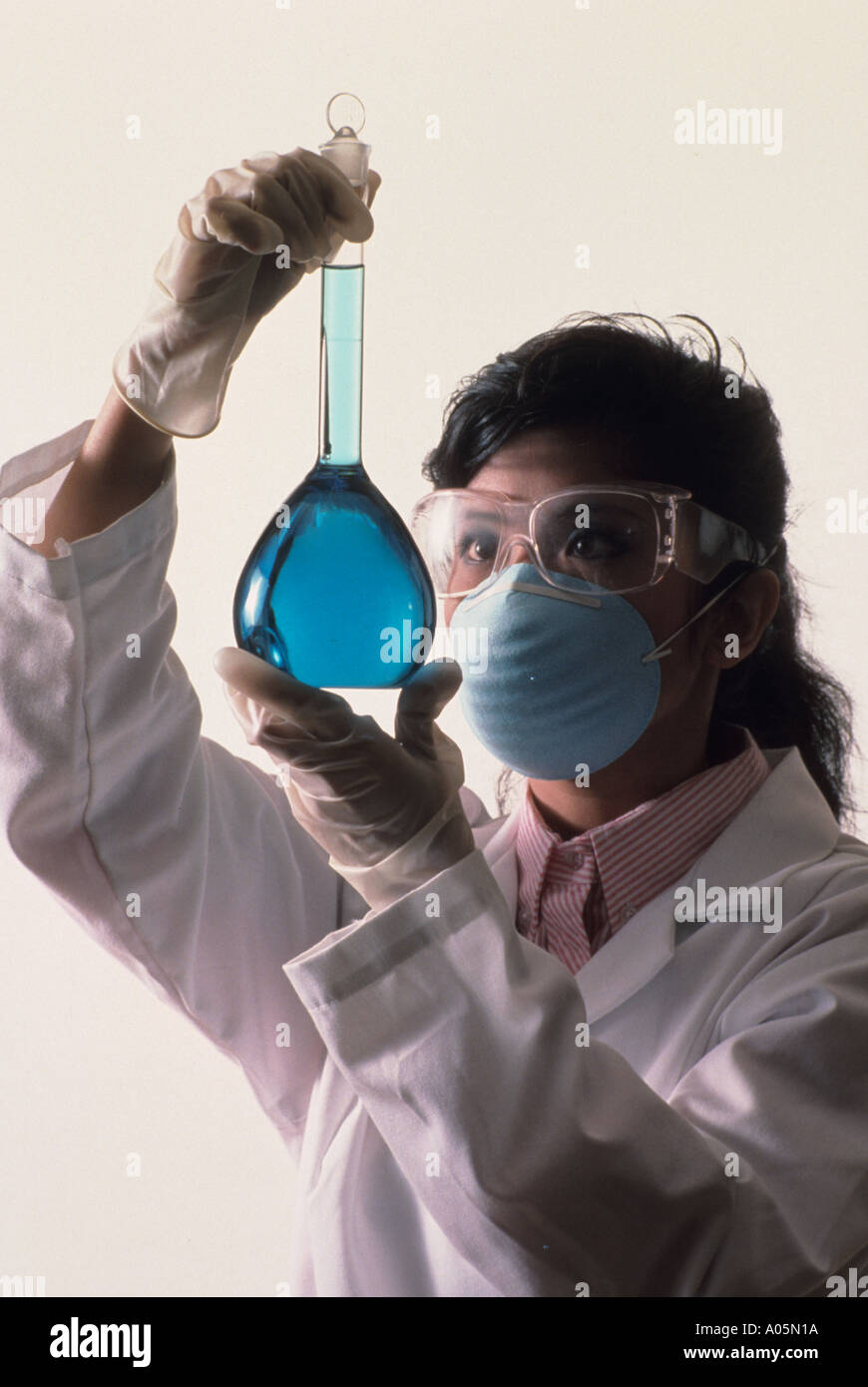 Female scientist wearing a face mask goggles and latex gloves holding a ...