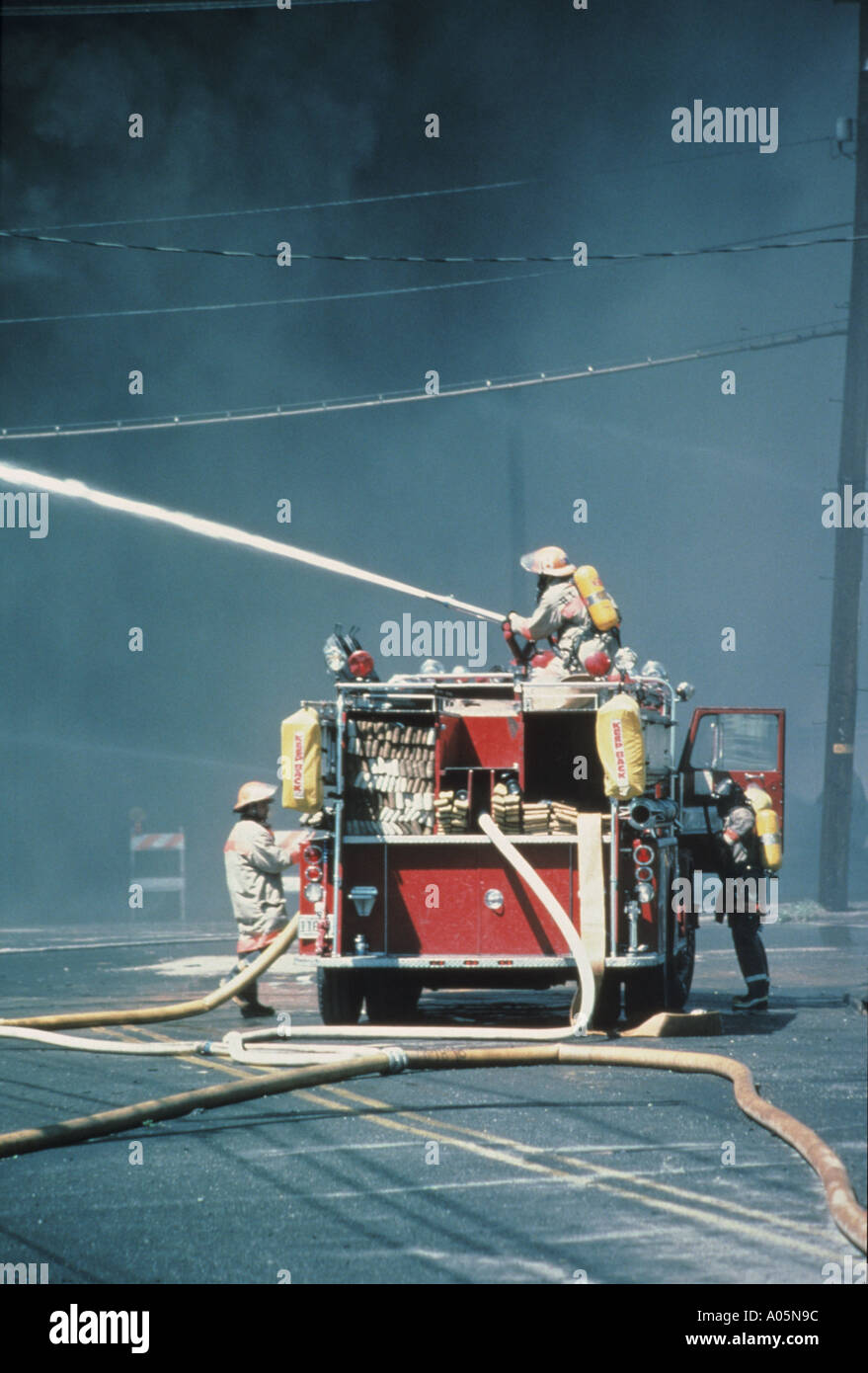 Smoky image of firefighters using the water hose on the fire truck to ...