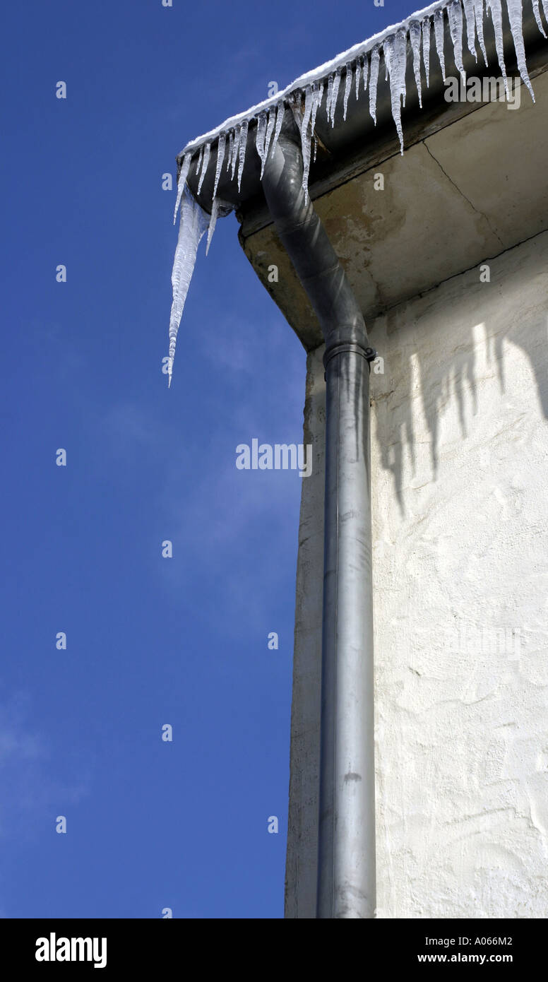A pipe is seen at the corner of a building with ice frozen on the roof ...