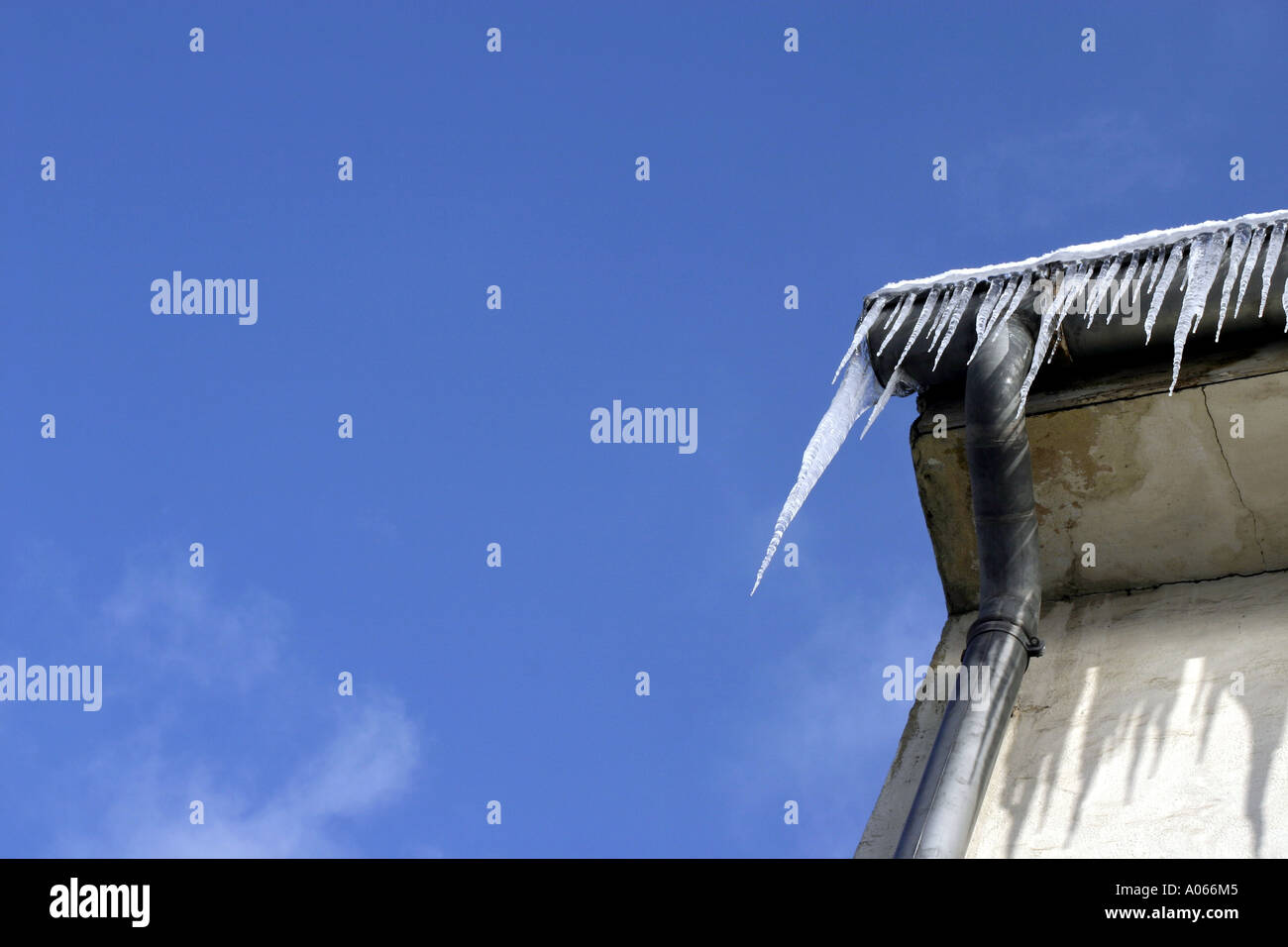 A pipe is seen at the corner of a building with ice frozen on the roof ...