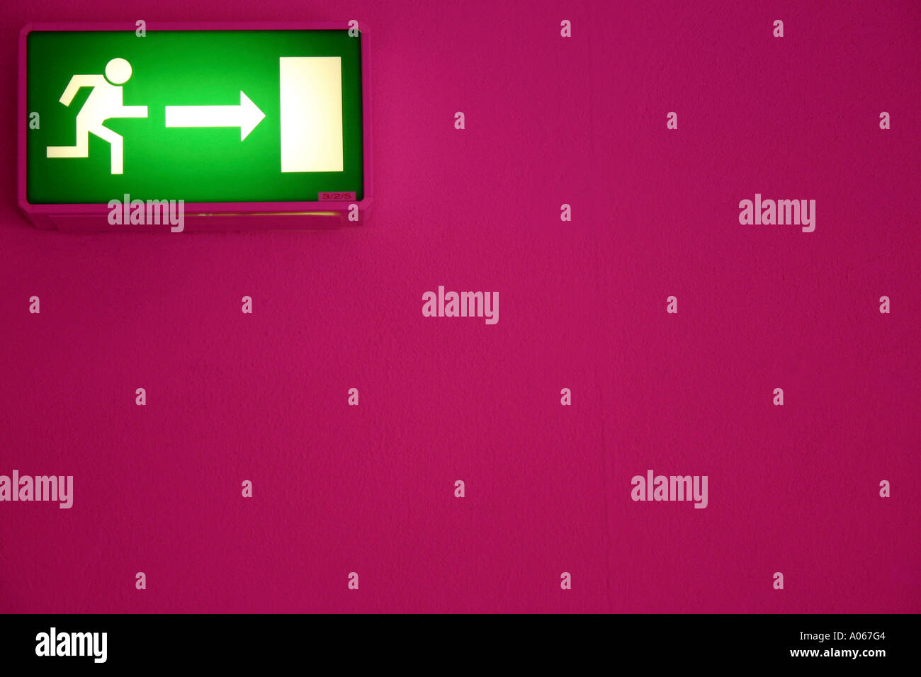Illuminated escape route board seen on a pink wall Stock Photo - Alamy