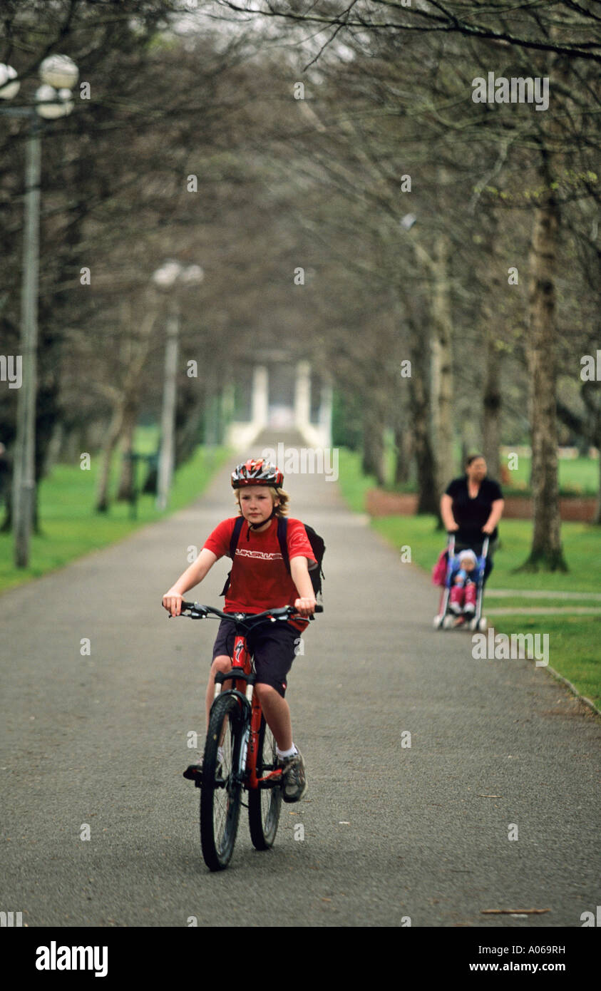 Boy cycling and a mother pushing a child in a push chair in Queens Park ...