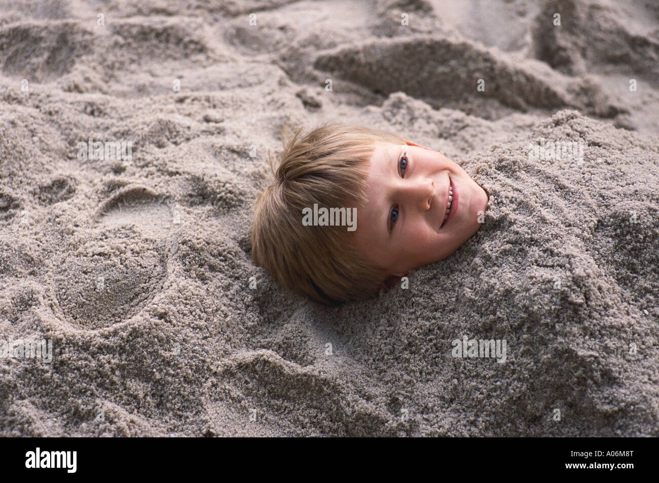 Six Year old blond haired boy buried in sand Stock Photo - Alamy