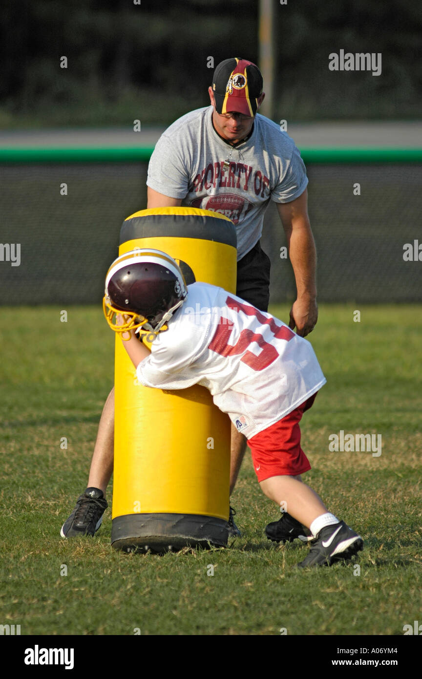 Coach talking to young kid at football practice with blocking dummy bag ...