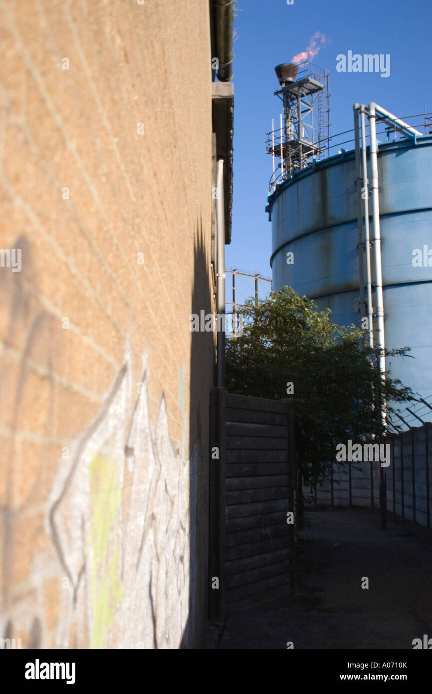 view of factory works along a brick wall, steel tank with flame burning ...