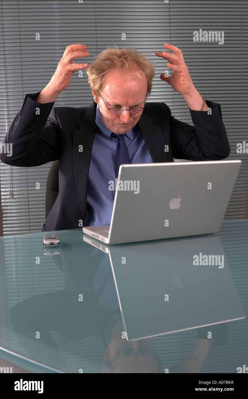 Businessman using a laptop computer looking stressed and holding his ...
