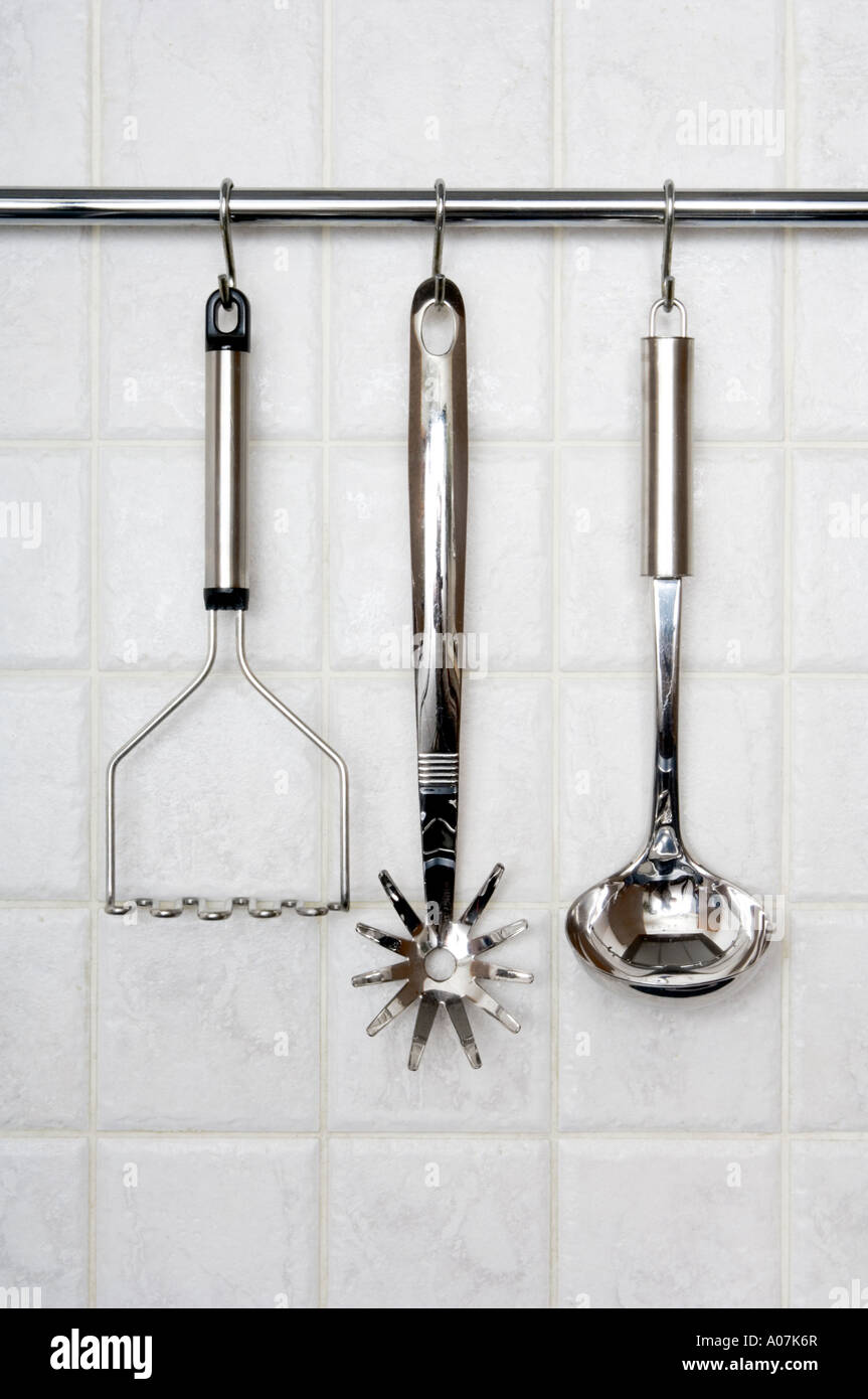Stainless steel kitchen utensils hanging on a rack, against white tiles ...