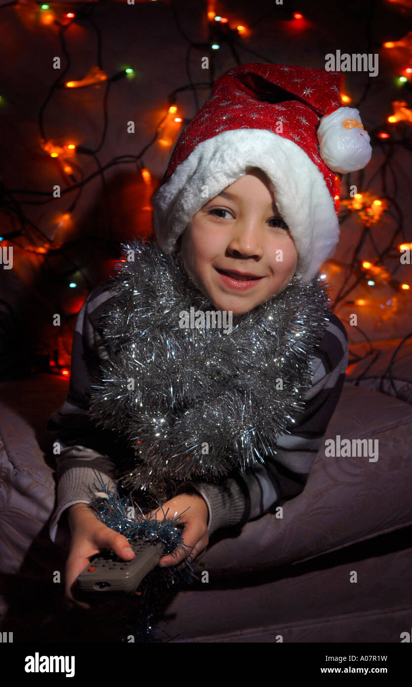 A young boy watching TV in santa hat with television remote control ...