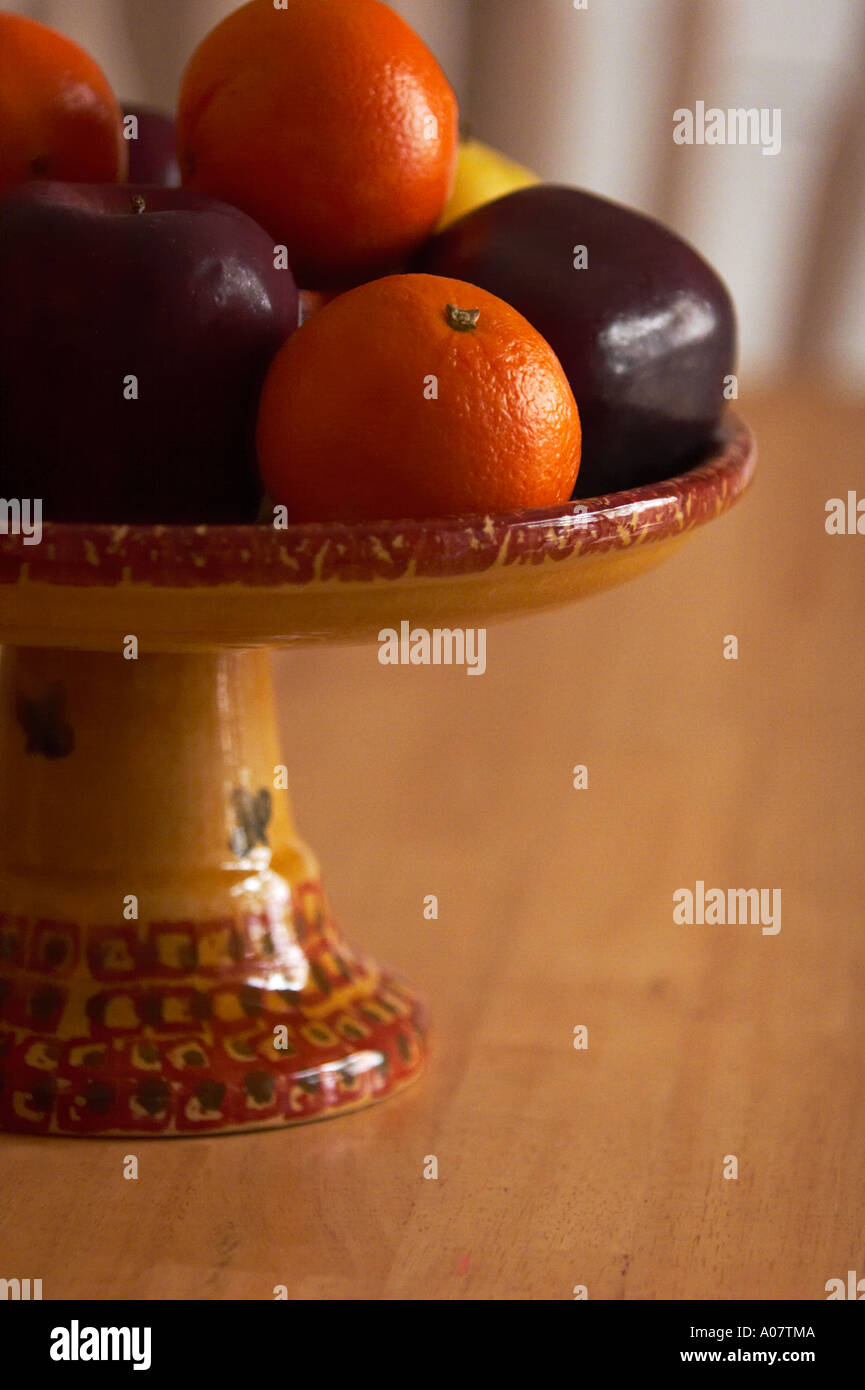 A platter of fruit, apples and oranges, on a table with a chair in the ...