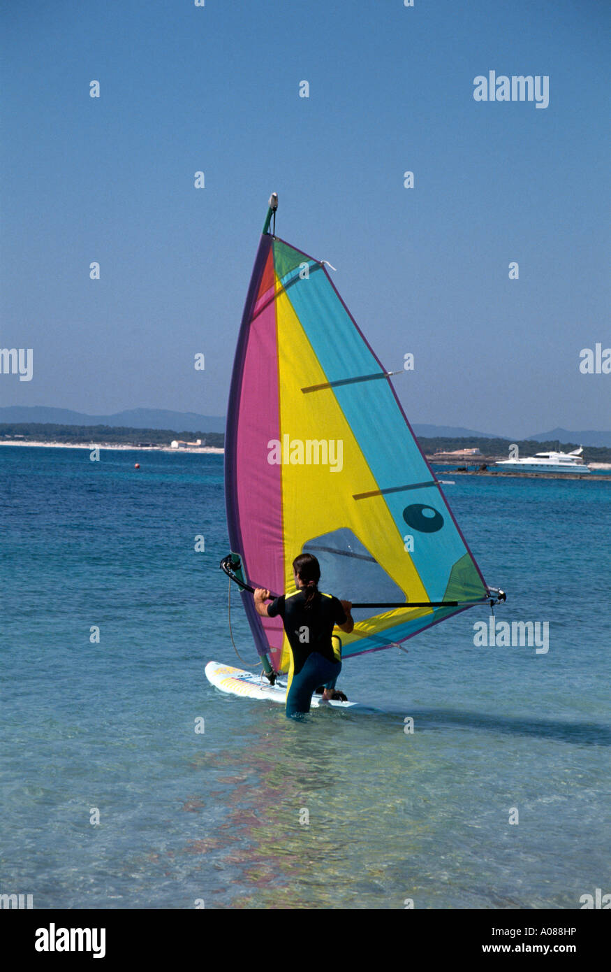 A windsurfer protected from the cold by a wet suit with one foot on his ...