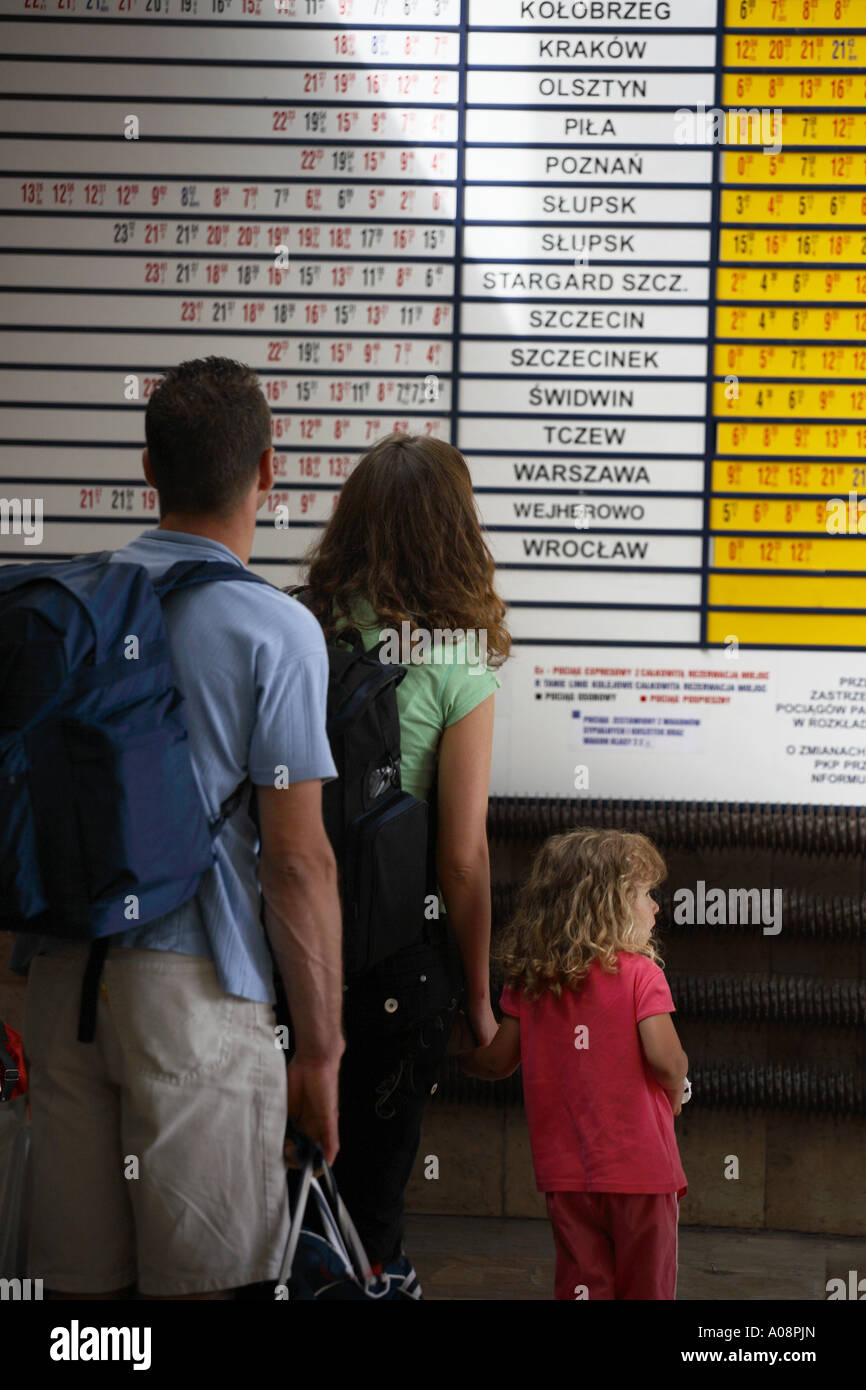A young family checking times from a timetable at a Polish railway ...
