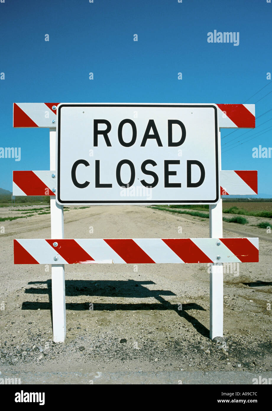 A red black and white road closed sign blocking a dirt road with a ...