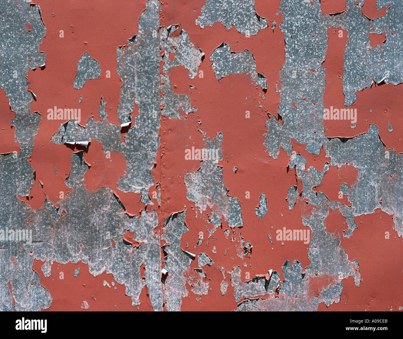 A close up of an aged and weathered riveted metal surface with pieces of bright red paint ...