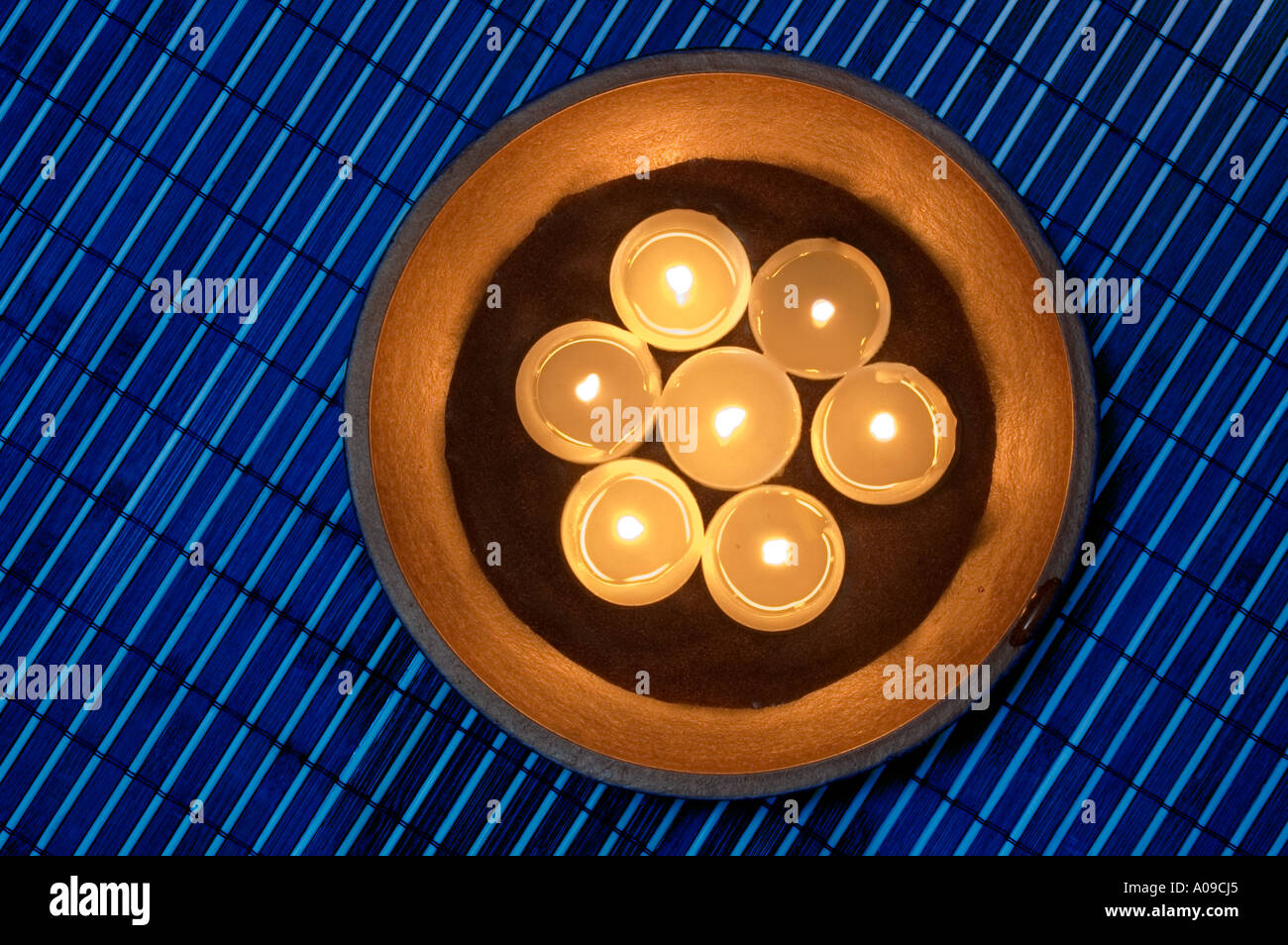 wooden bowl containing several small tealight candles lit on japanese ...