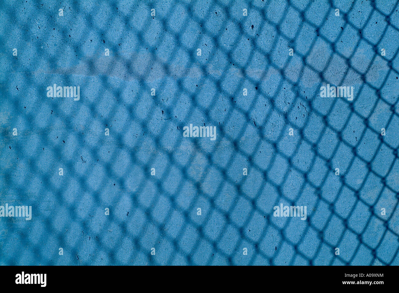 A chain link fence shadow forms a pattern on a blue wall. Urban ...