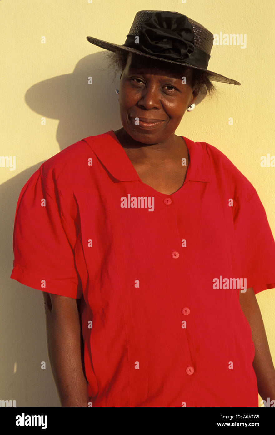 CARIBBEAN BAHAMAS Bahamian lady in red dress and straw hat smiling at ...