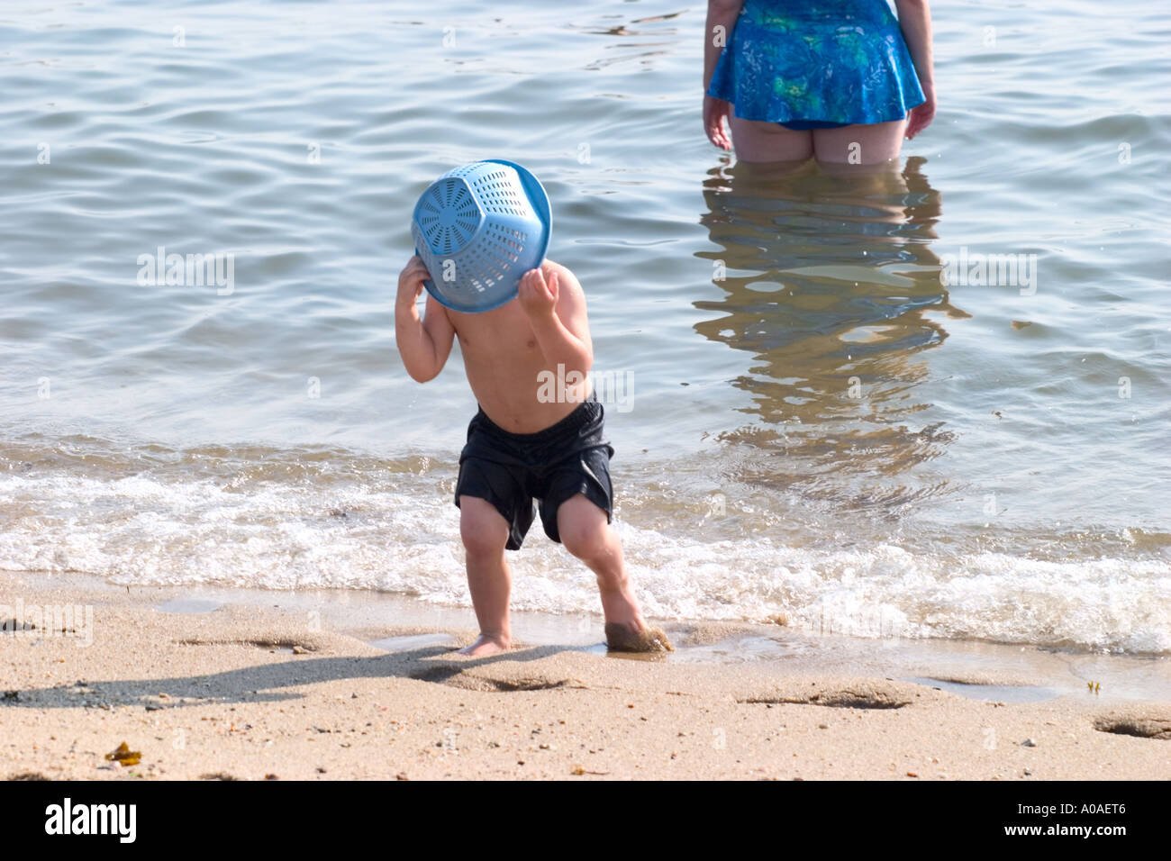 Young boy with a plastic food drainer over his head walking on the sand ...