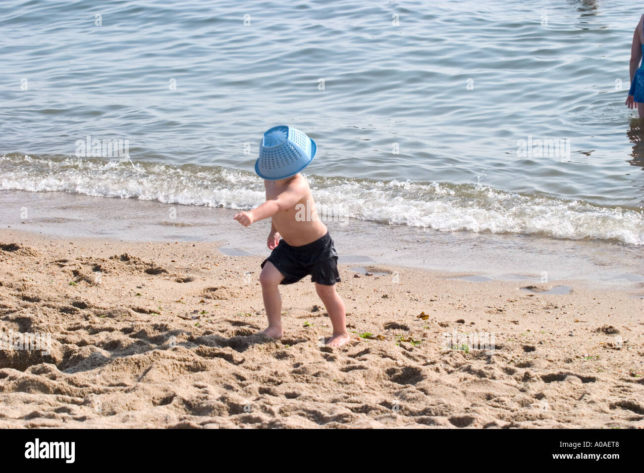 Young boy with a plastic food drainer over his head walking on the sand ...