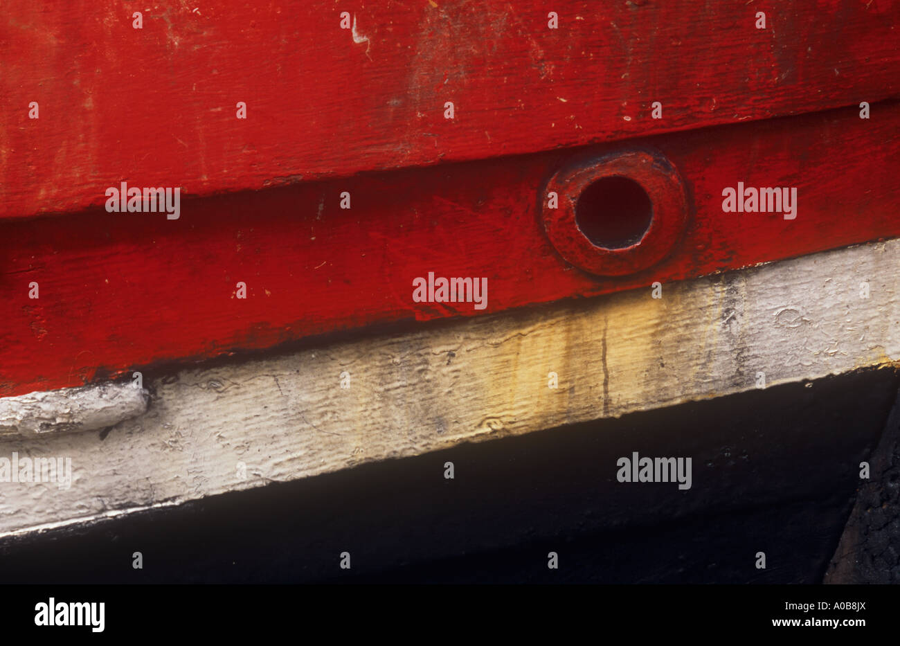 Detail of timber hull of boat brightly painted red white and black but ...