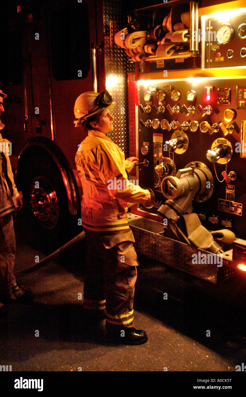 A female firefighter engineer operates the pump panel at a night time ...
