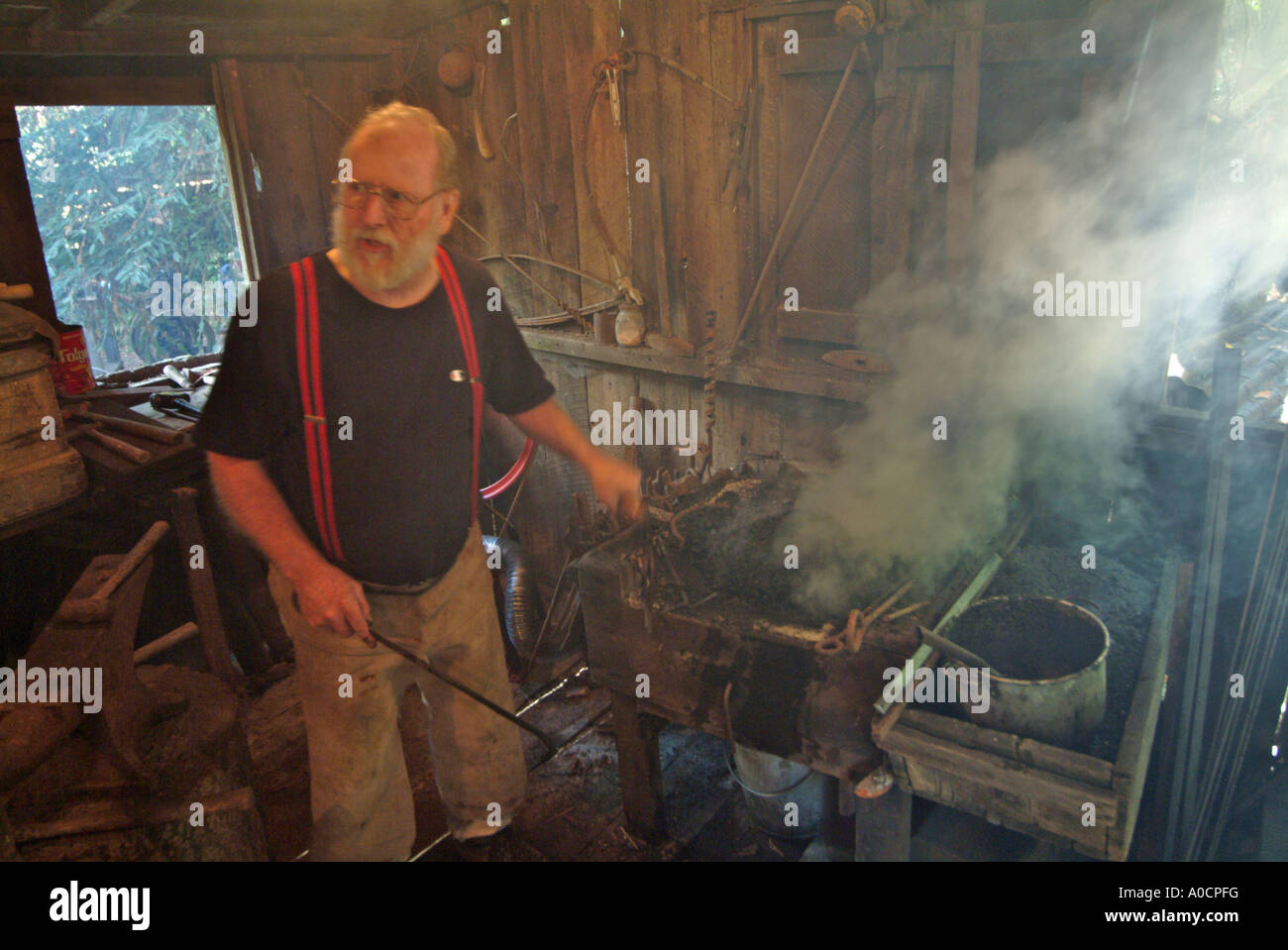 A blacksmith prepares the coal fed fire before working on a metal tool ...