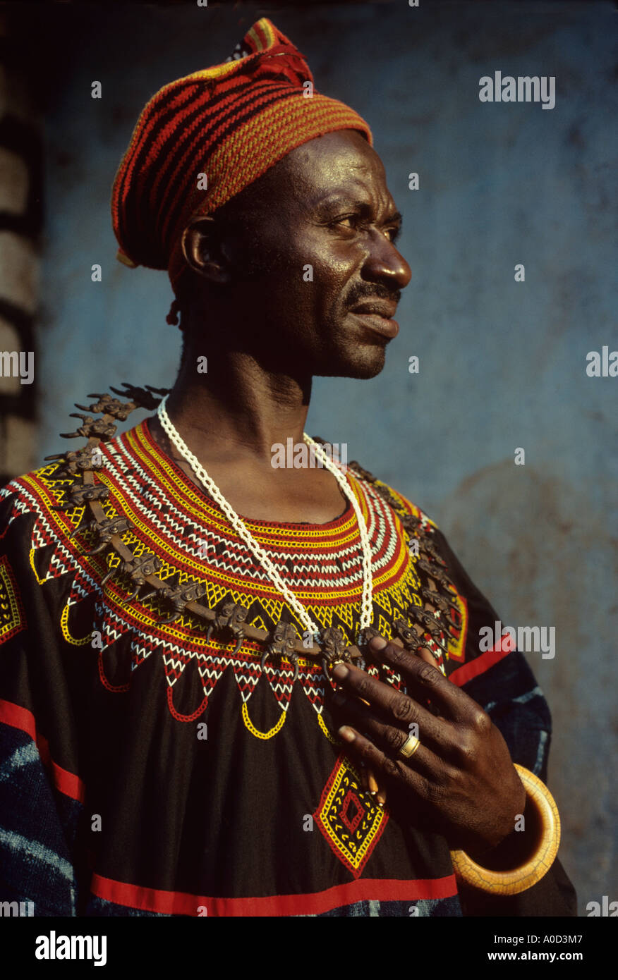Bamun man in ceremonial dress wears a heavy bronze collar with shapes ...
