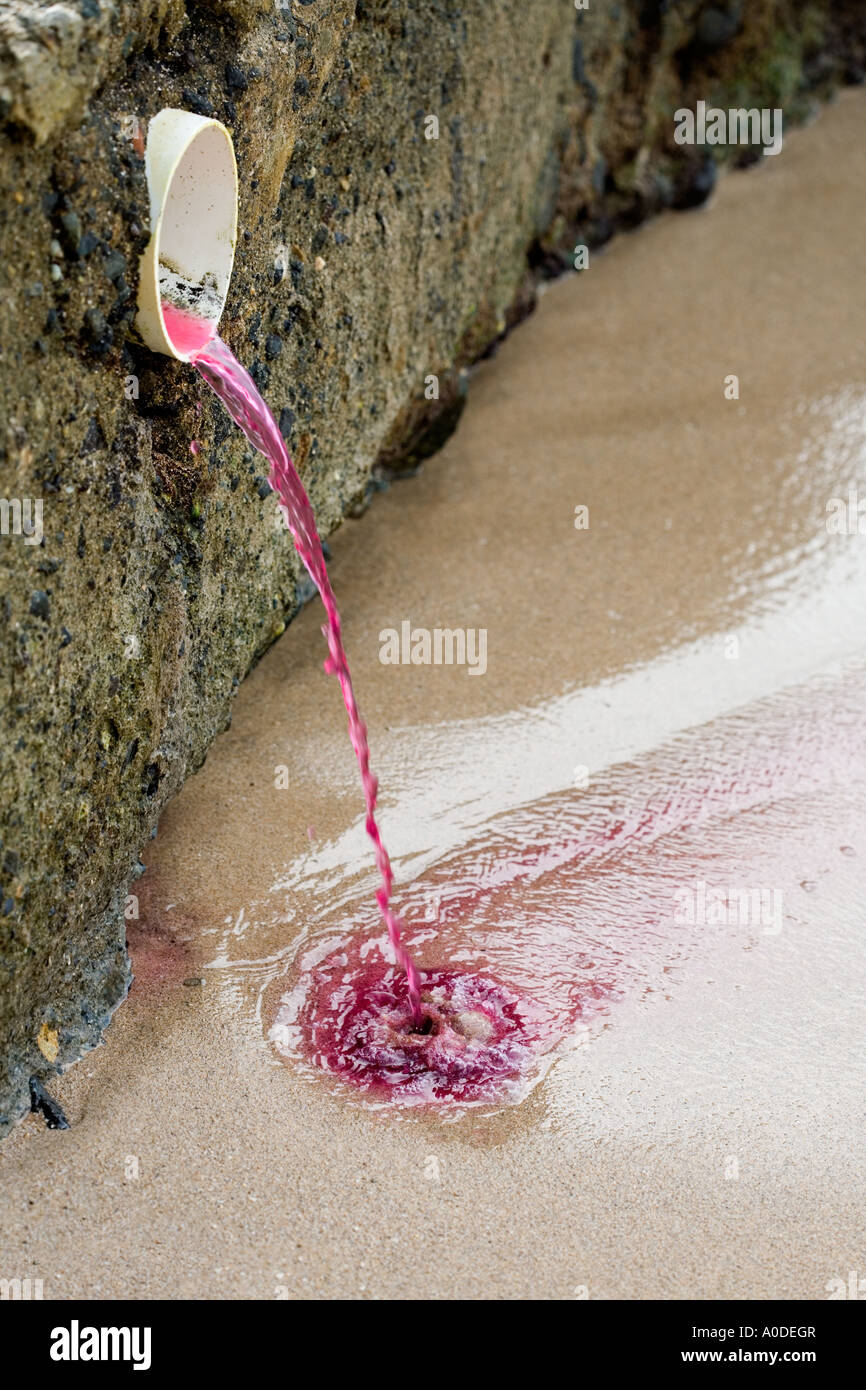Drainage pipe pouring pink liquid on to beach Stock Photo - Alamy
