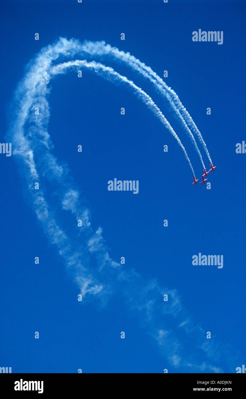 Four small red aeroplanes looping the loop and trailing white smoke ...