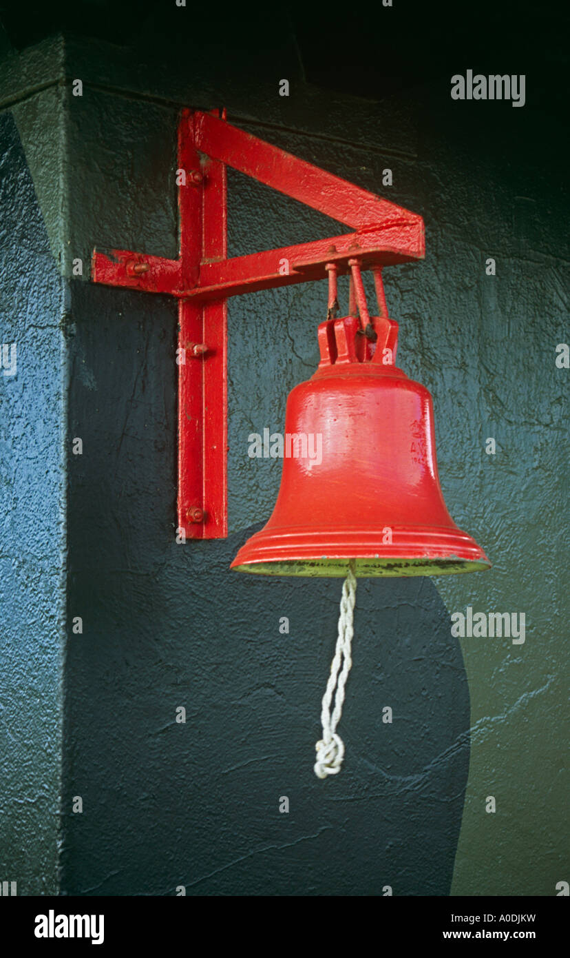 Bright red fire bell mounted on corner of wall of camouflaged building ...
