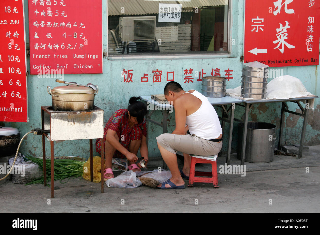 Man and a woman preparing food on the pavement in a Beijing side street ...
