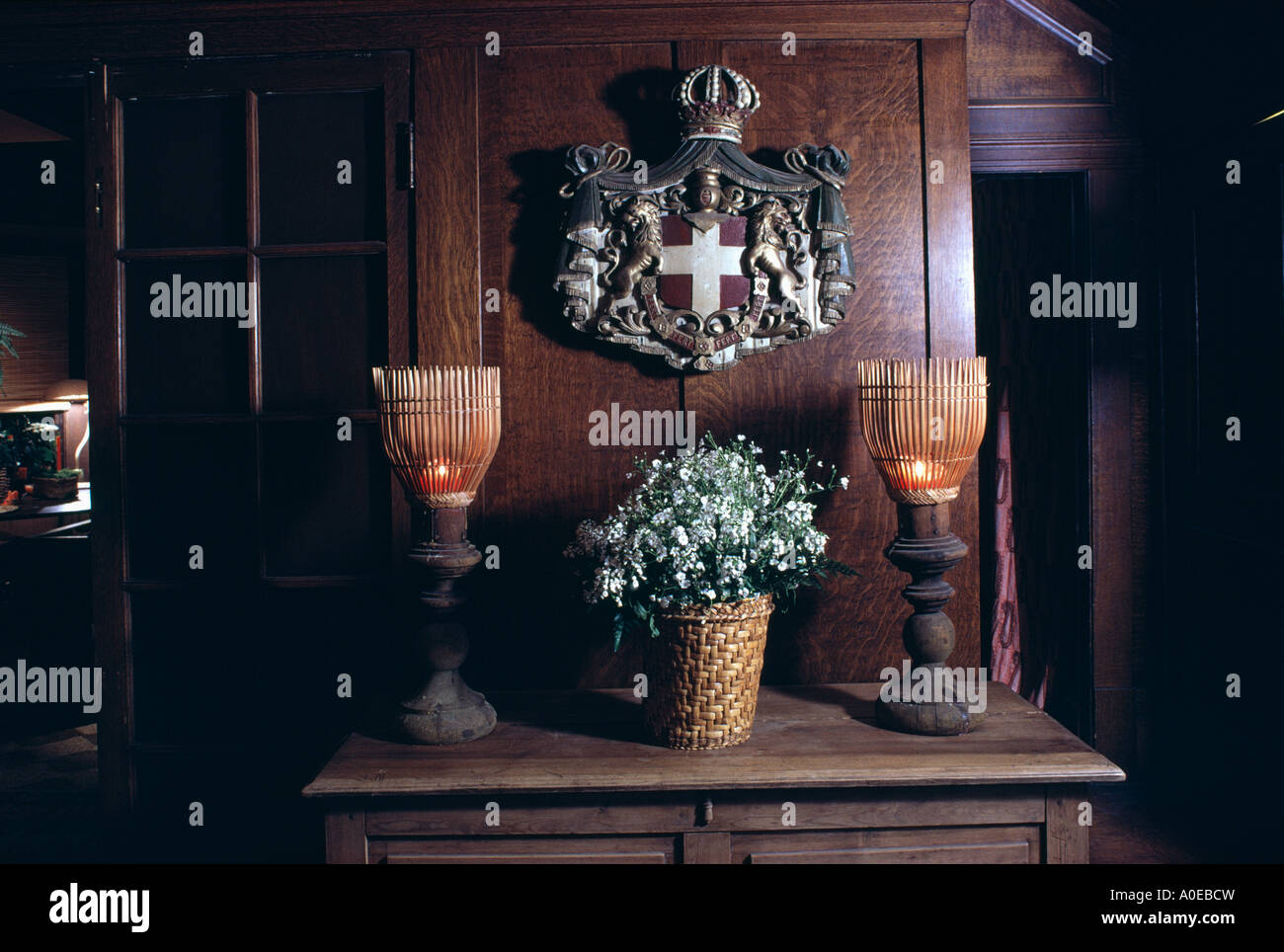 Shield on panelling above table with lighted lamp and flowering plant ...