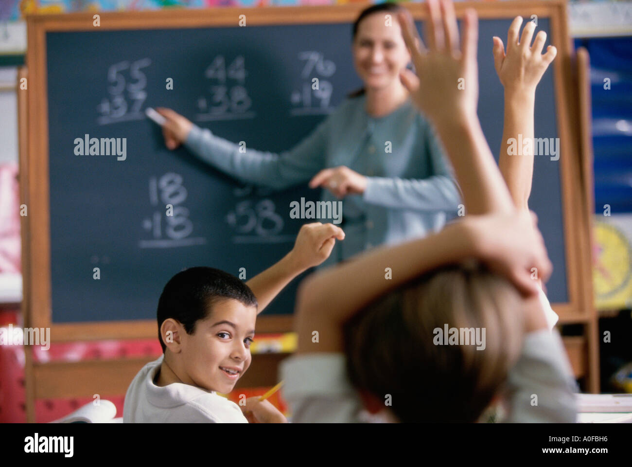 Female teacher pointing to a chalkboard in a classroom with her ...