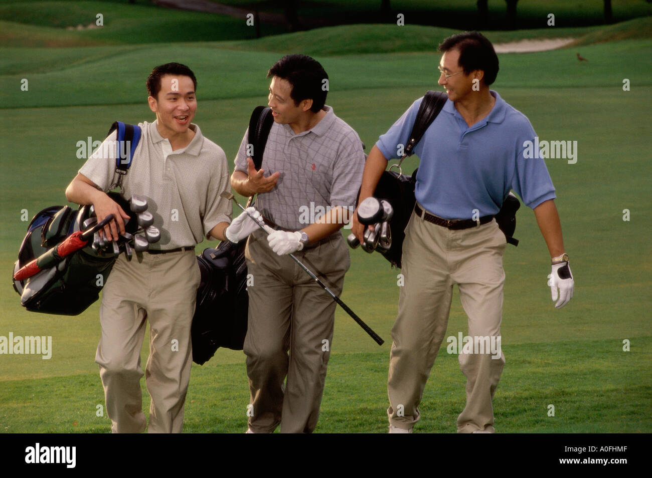 Three men carrying golf bags at a golf course Stock Photo - Alamy