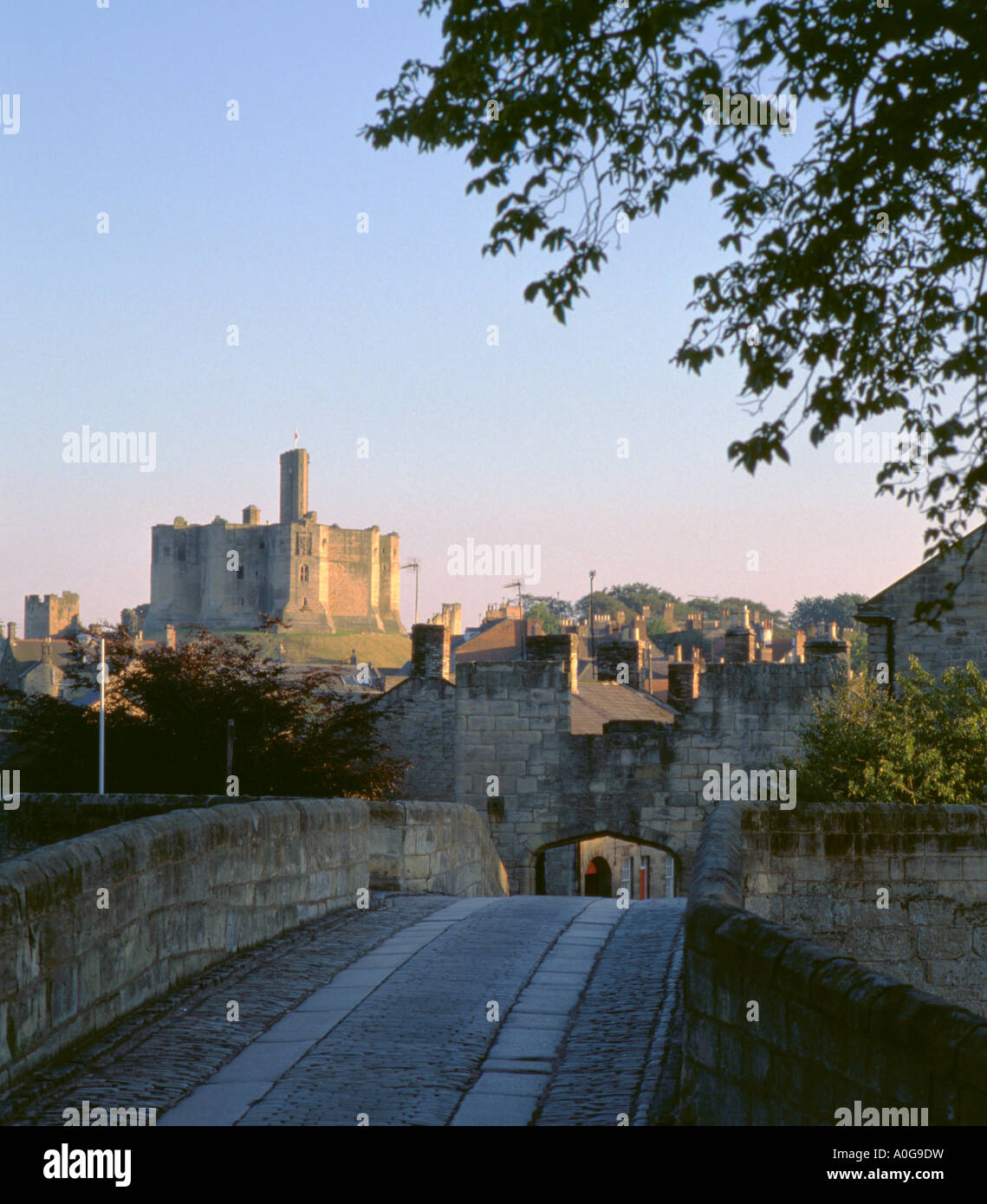 Old fortified bridge with village and castle beyond at sunset ...