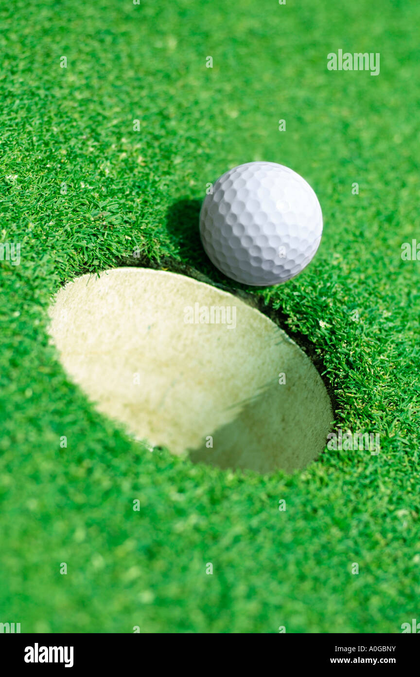 Golf ball on edge of hole on golf green Stock Photo - Alamy