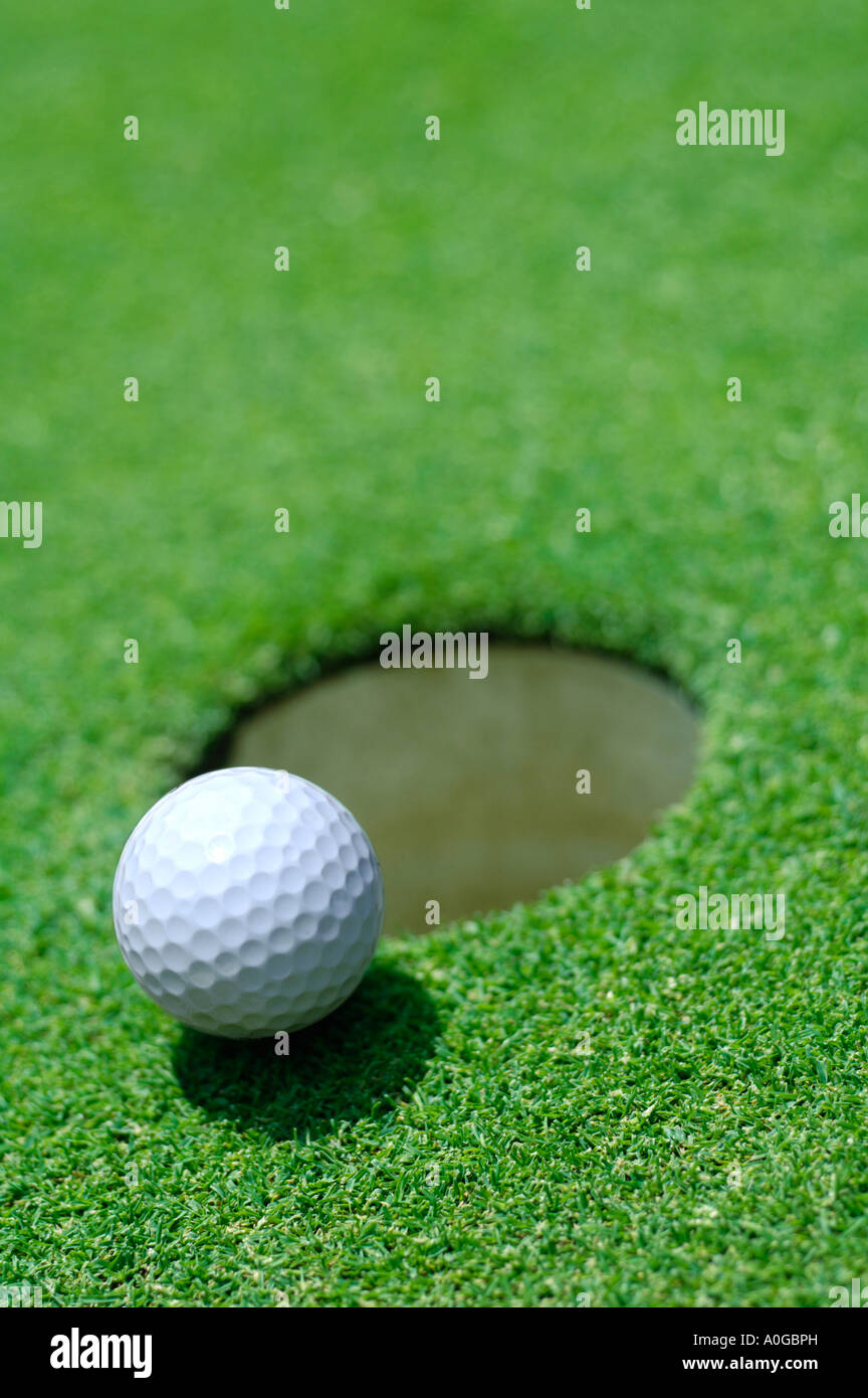 Golf ball on edge of hole on golf green Stock Photo - Alamy