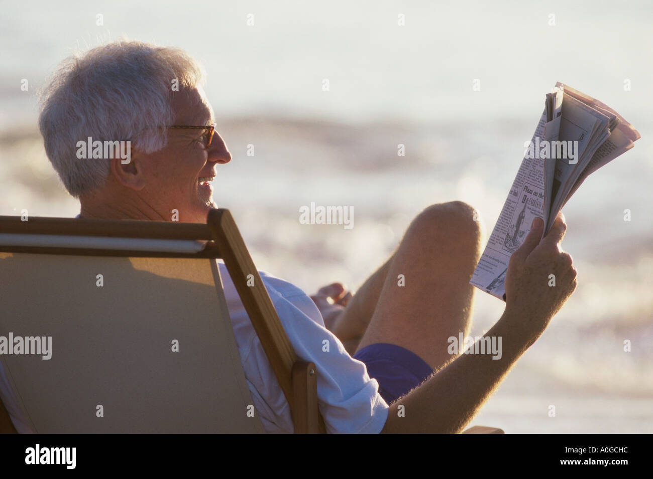 Rear view of a senior man reading a newspaper on the beach Stock Photo ...