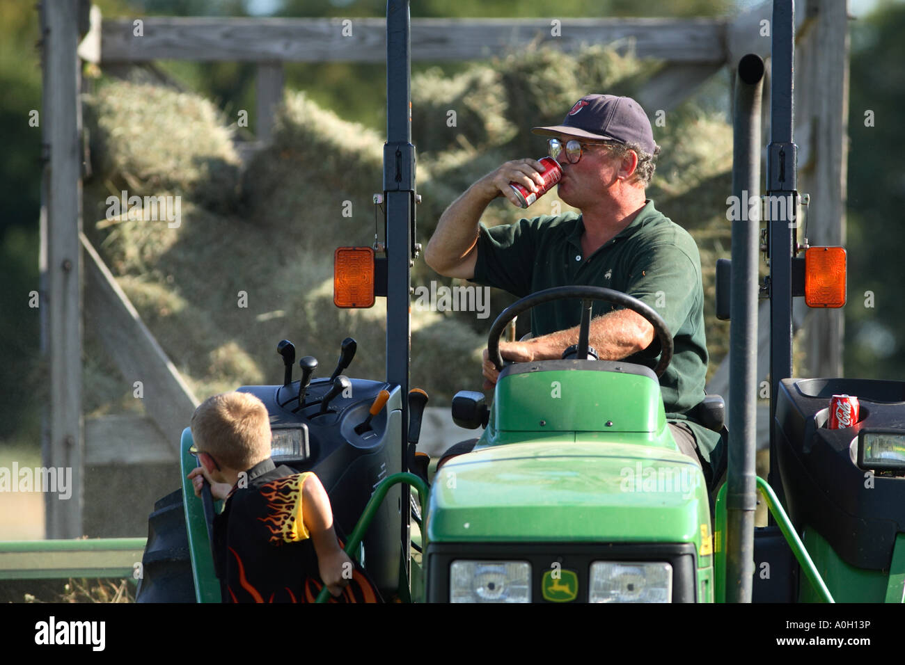 A farmer drinks a Coke while he pulls a hay wagon A boy rides with him ...