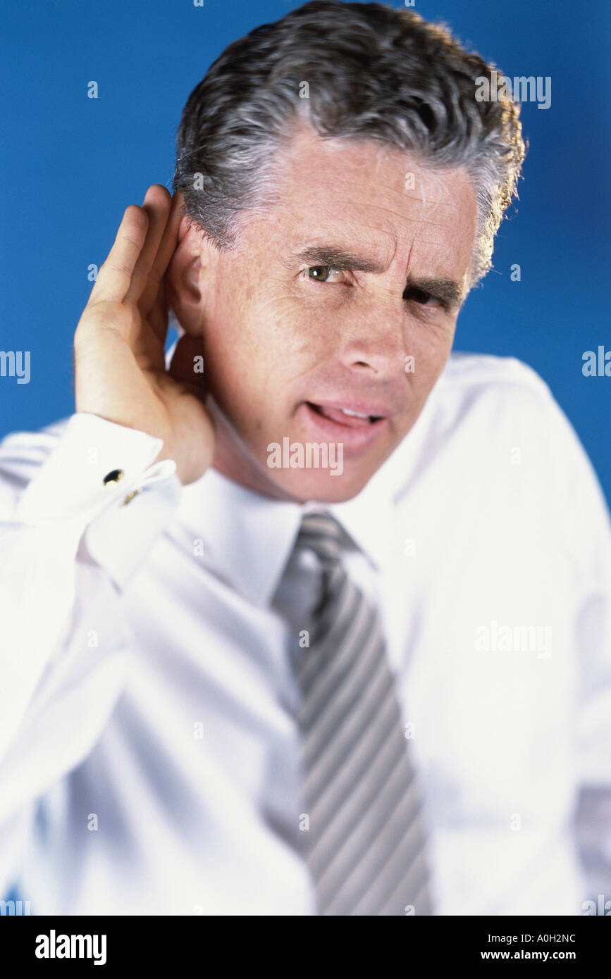 Mid adult man putting his hand behind his ear in an effort to hear ...