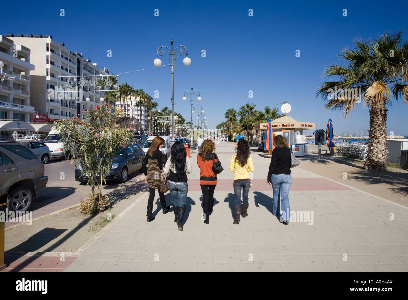 A BACK VIEW OF LOCAL GIRLS WALKING ALONG THE LARNAKA TOWN SEAFRONT IN ...