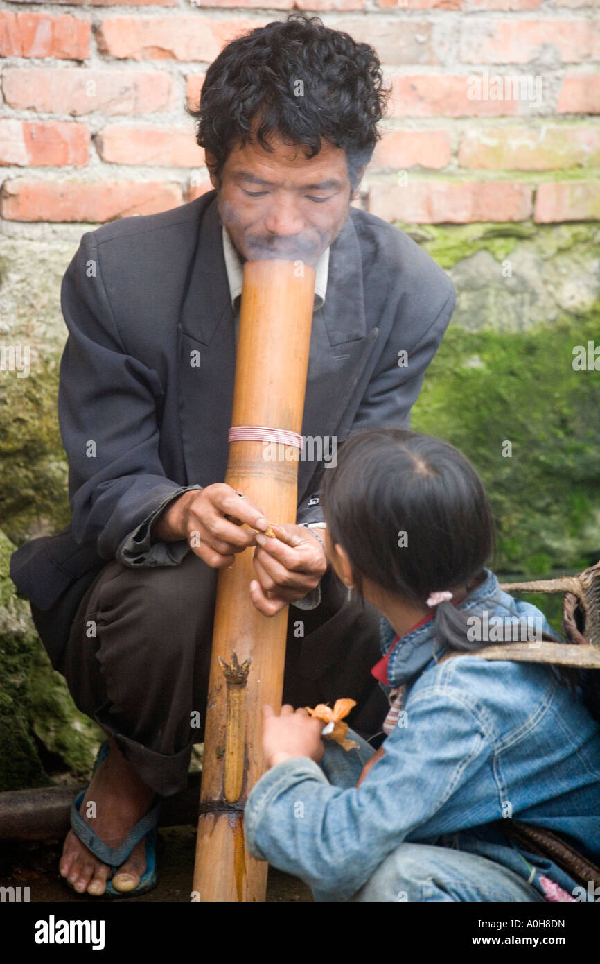 Young girl watching man smoke tobacco in a bamboo bong, Shengcun ...