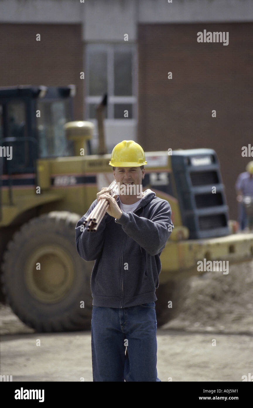 Portrait of a construction worker carrying metal pipes on his shoulder ...